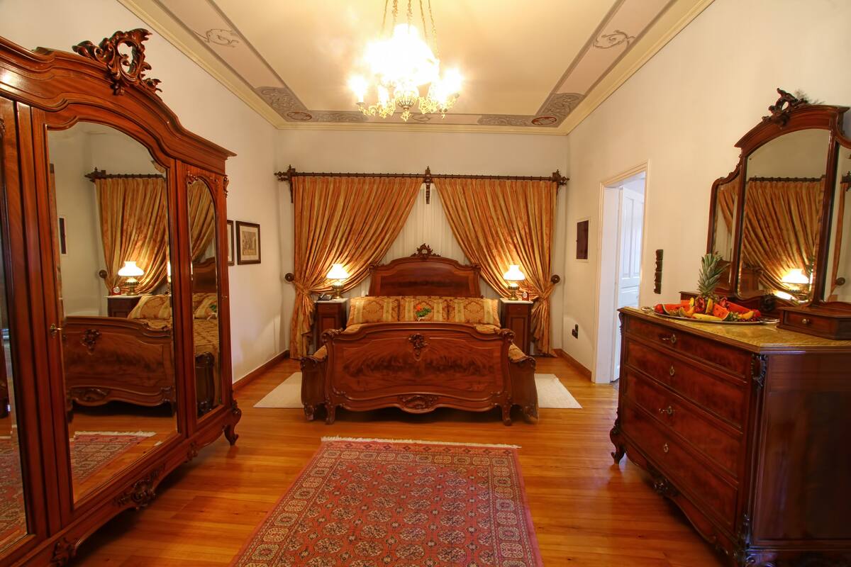 Quarto tradicional com uma cama grande, móveis de madeira elaborados e um candelabro.