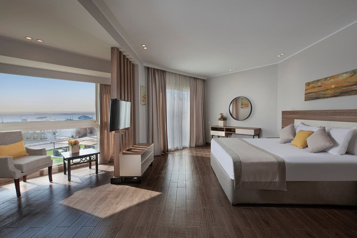 Quarto de hotel moderno com uma cama grande, uma escrivaninha, uma TV e vista para a cidade.