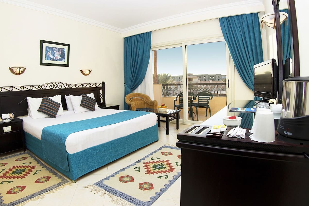 Quarto de hotel com cama, escrivaninha com cafeteira, televisão e vista para a cidade.