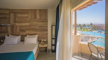 Quarto de hotel com cabeceira de madeira, cama com roupa de cama branca, mesa de cabeceira com abajur e vista para a piscina e área do resort.