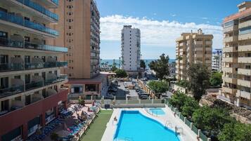 Um hotel com piscina, várias varandas e vista para o mar.