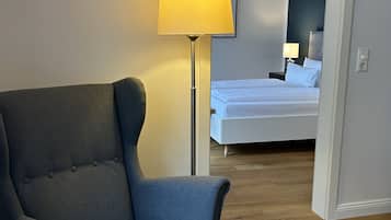 Quarto com poltrona azul, luminária de cabeceira e cama com roupa de cama branca.