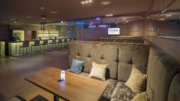 Uma área de bar com balcão, banquetas e um espaço de estar com sofá e mesa.