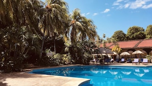 Uma piscina com espreguiçadeiras, palmeiras e um edifício com telhado vermelho.