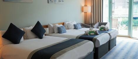 Quarto de hotel com duas camas, um sofá, uma luminária e vista para o exterior.