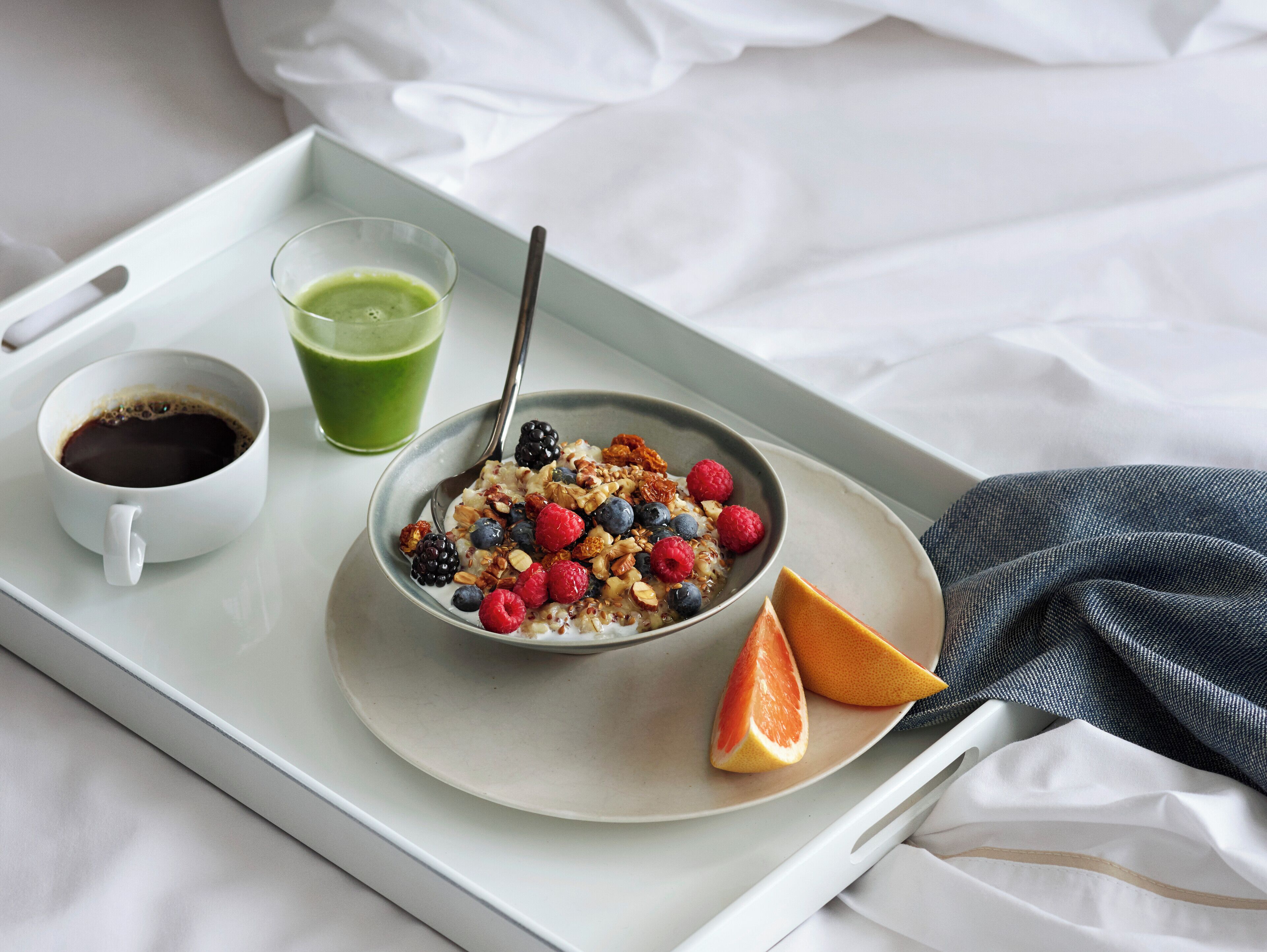 Uma bandeja de café da manhã com uma tigela de cereal, uma xícara de café, um copo de suco verde e duas metades de uma toranja.