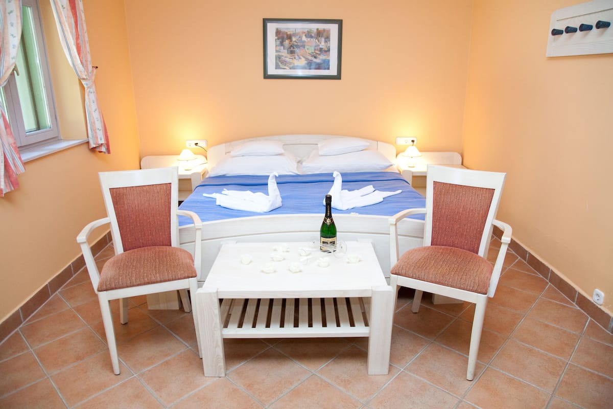Quarto de hotel com uma cama, duas cadeiras, uma mesa e uma garrafa de champanhe.