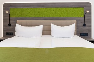 Quarto de hotel moderno com parede coberta de musgo verde, cabeceira bege e duas luminárias de cabeceira.