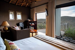 Quarto de hotel com cama, escrivaninha, cadeira, estante de livros e uma grande janela com vista para o exterior.