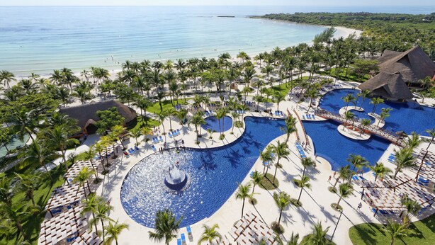 Resort com uma grande piscina central, piscinas menores e área de praia.