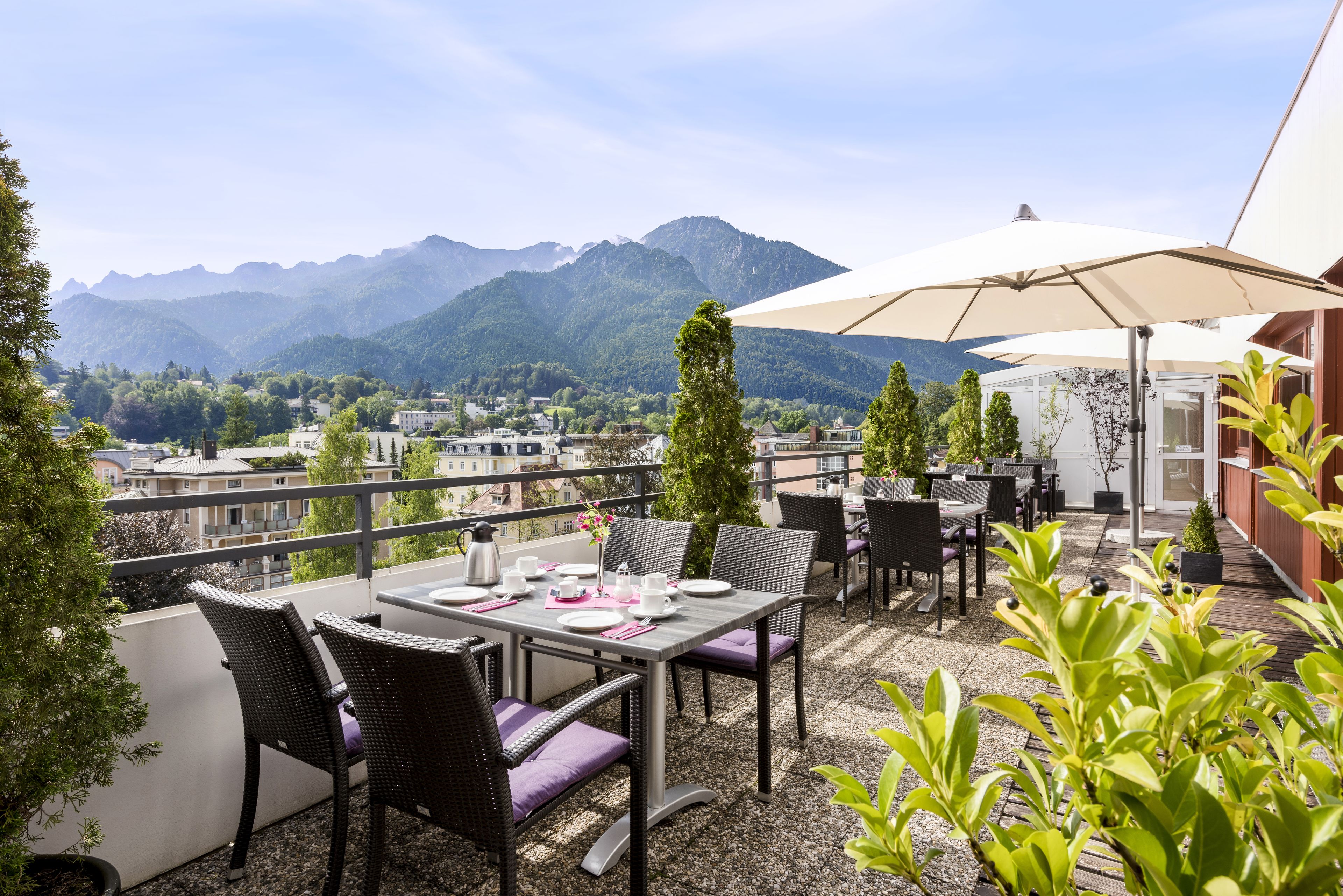 Um terraço com área de estar ao ar livre, uma mesa posta para refeições e vista para montanhas ao fundo.