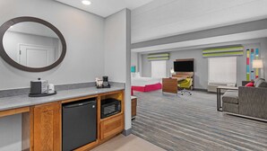 Quarto de hotel com cozinha compacta, um espelho grande, televisão de tela plana, sofá e uma pequena mesa de jantar.