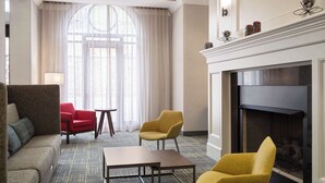 Um hall de hotel com lareira, um sofá, uma poltrona vermelha, uma poltrona amarela e uma mesinha.