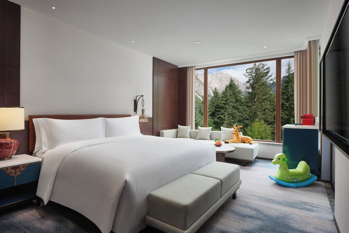 Quarto de hotel moderno com uma cama grande, um sofá, uma mesinha e uma televisão.