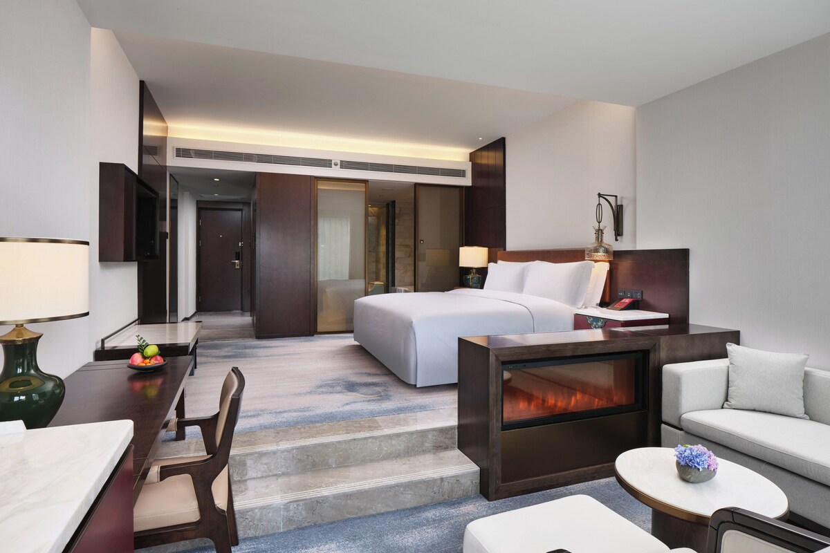 Quarto de hotel com uma cama, uma escrivaninha, uma cadeira, um sofá e uma pequena mesa com um vaso.