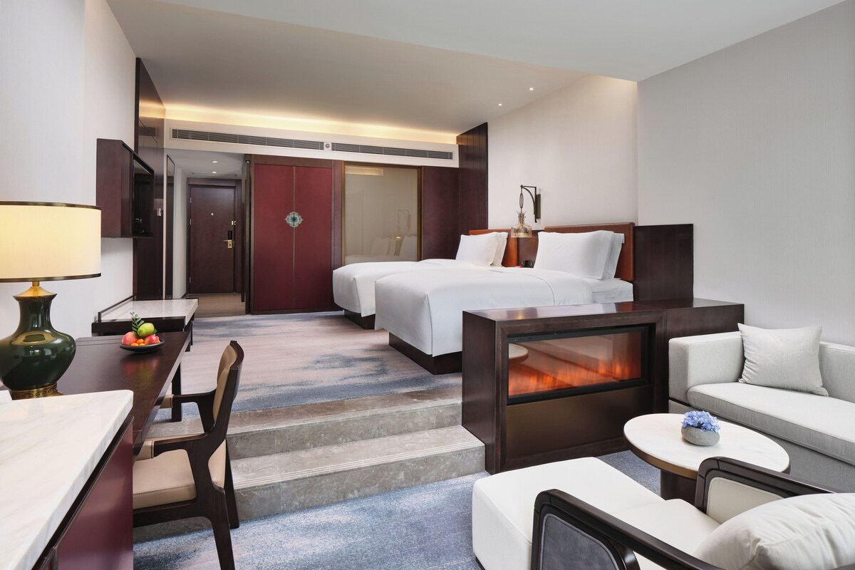 Quarto de hotel com cama, escrivaninha, poltrona, sofá e pequena mesa com abajur.