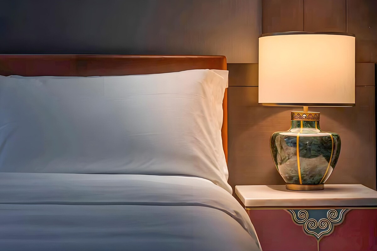 Cama bem arrumada com lençóis brancos, luminária decorativa com base de mármore e cabeceira de madeira.