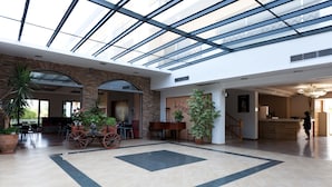 Um hall espaçoso com teto alto, um piano, plantas em vasos e uma ampla área aberta com piso estampado.