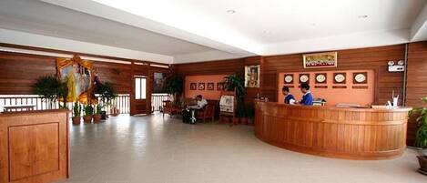 Um saguão de hotel com uma recepção de madeira, uma pintura grande e vários relógios na parede.