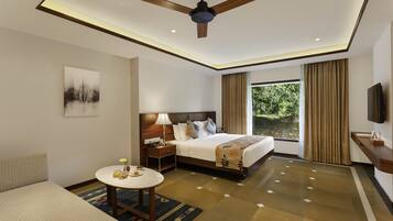Quarto de hotel com cama, mesa de cabeceira, luminária e vista para o verde lá fora.