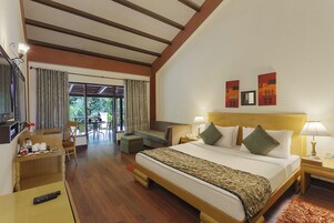 Quarto de hotel com cama grande, escrivaninha, cadeira, televisão e varanda com cortinas.