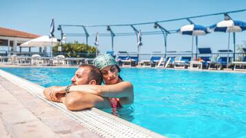 Piscina com espreguiçadeiras e guarda-sóis ao fundo.