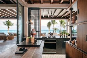 Uma cozinha moderna com vista para o oceano, destacando uma bancada de madeira, fogão embutido e diversos eletrodomésticos.