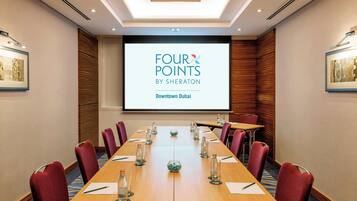 Uma sala de conferências com uma mesa comprida, cadeiras vermelhas e uma tela exibindo "FOUR POINTS BY SHERATON Downtown Dubai".