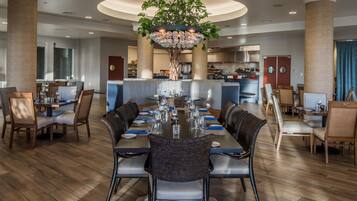 Uma ampla sala de jantar com uma mesa comprida, várias cadeiras e um lustre central.