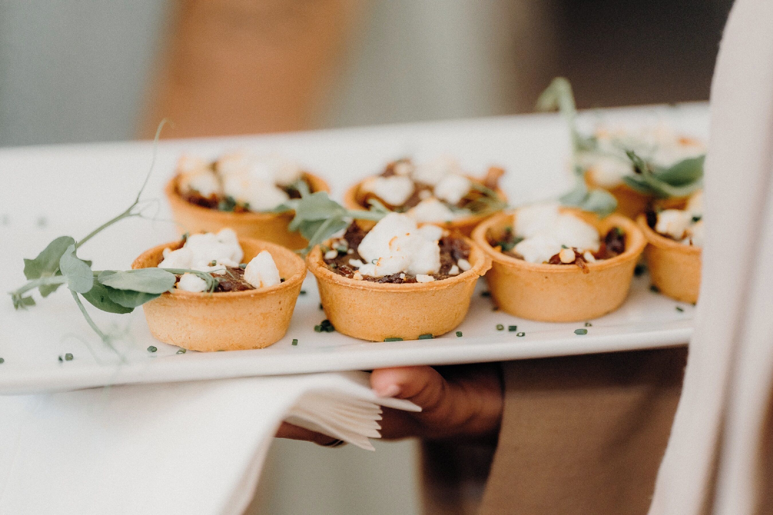 Uma bandeja de mini quiches com um enfeite, sendo segurada por alguém.