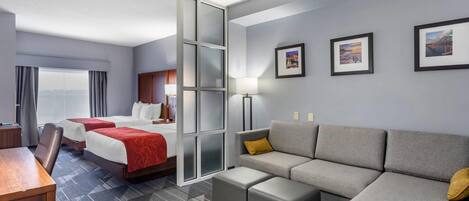 Quarto de hotel com cama, duas mesas de cabeceira, sofá, escrivaninha e uma janela grande.