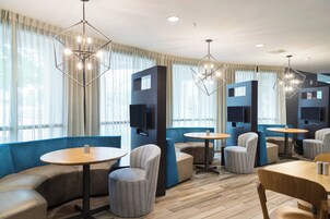 Um saguão de hotel moderno com áreas de estar, mesas redondas e uma grande tela de televisão.
