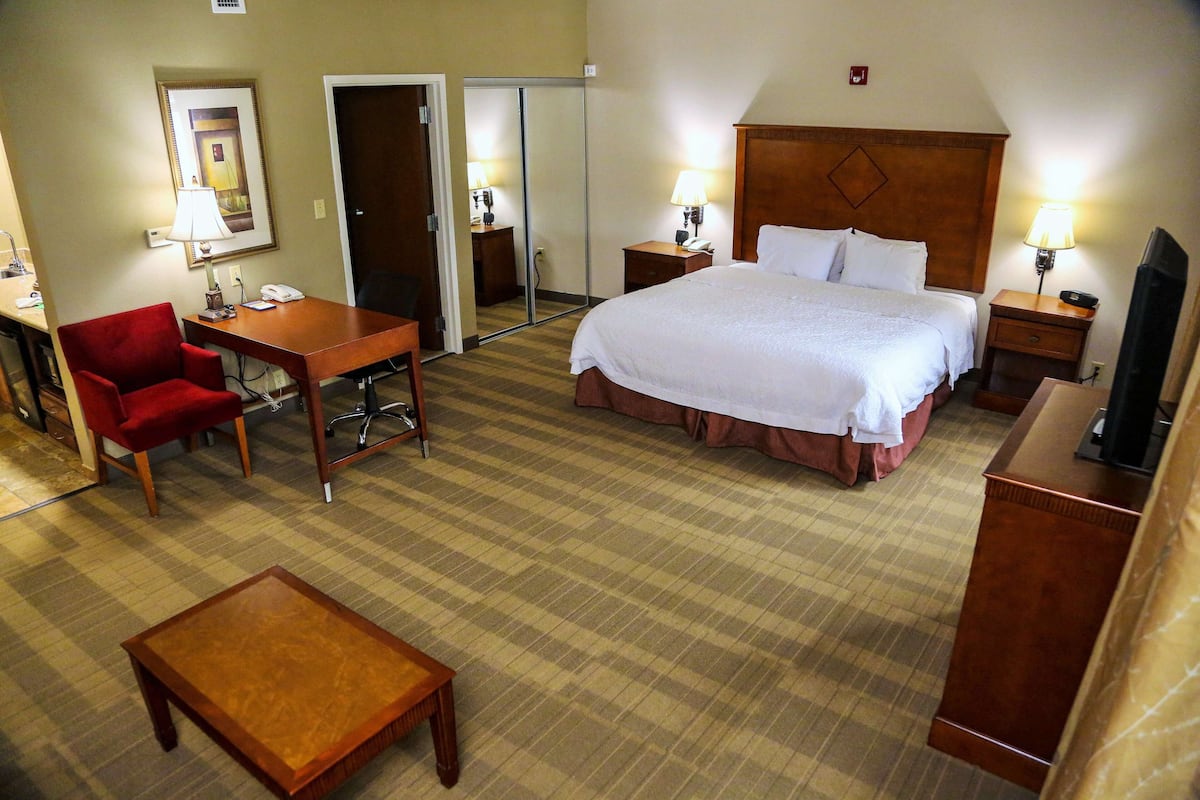 Quarto de hotel com cama, escrivaninha, cadeira, televisão e espelho.