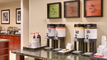 Uma área de recepção de hotel com um canto de café, obras de arte emolduradas e um balcão com diversos serviços.