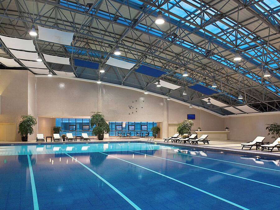 Piscina interior com várias pistas, espreguiçadeiras e plantas em vasos.