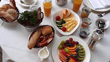 Mesa de café da manhã com diversos alimentos, incluindo pão, frutas e bebidas.
