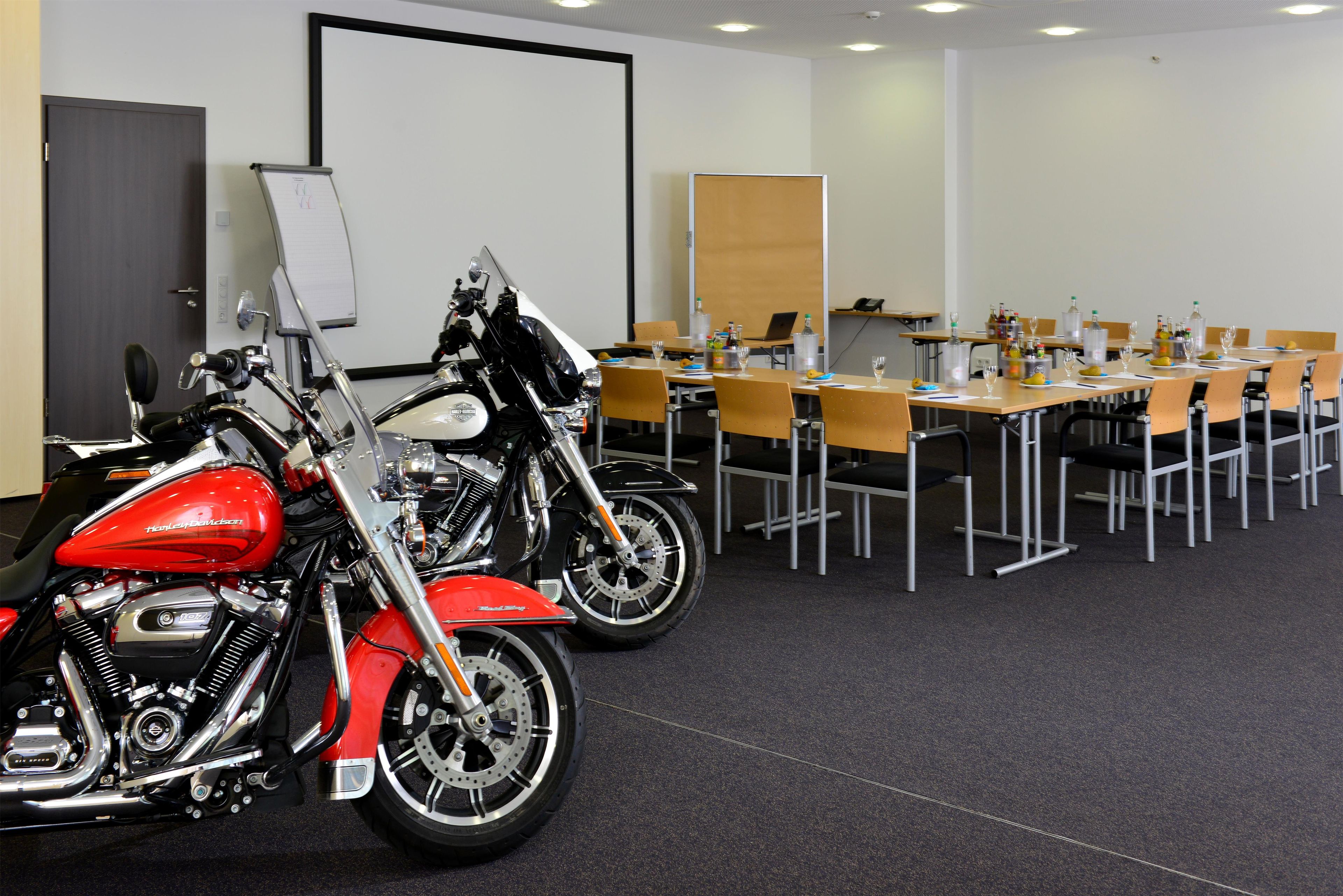 Sala de conferências com mesas, cadeiras e duas motocicletas.