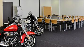 Sala de conferências com mesas, cadeiras e duas motocicletas.