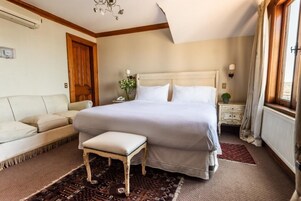 Quarto com uma cama grande, uma mesa de cabeceira, uma luminária e uma cadeira, além de uma janela com cortinas.