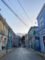 Uma rua de paralelepípedos ladeada por edifícios coloridos, uma placa de proibido fumar e uma vista distante de uma torre de igreja.
