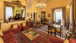 Uma sala de estar espaçosa com lustre, sofás vermelhos, área de jantar com mesa e cadeiras, e um espelho grande na parede.