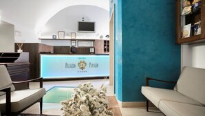 Uma área de recepção de hotel com balcão, televisão e espaço de estar com sofá e poltronas.