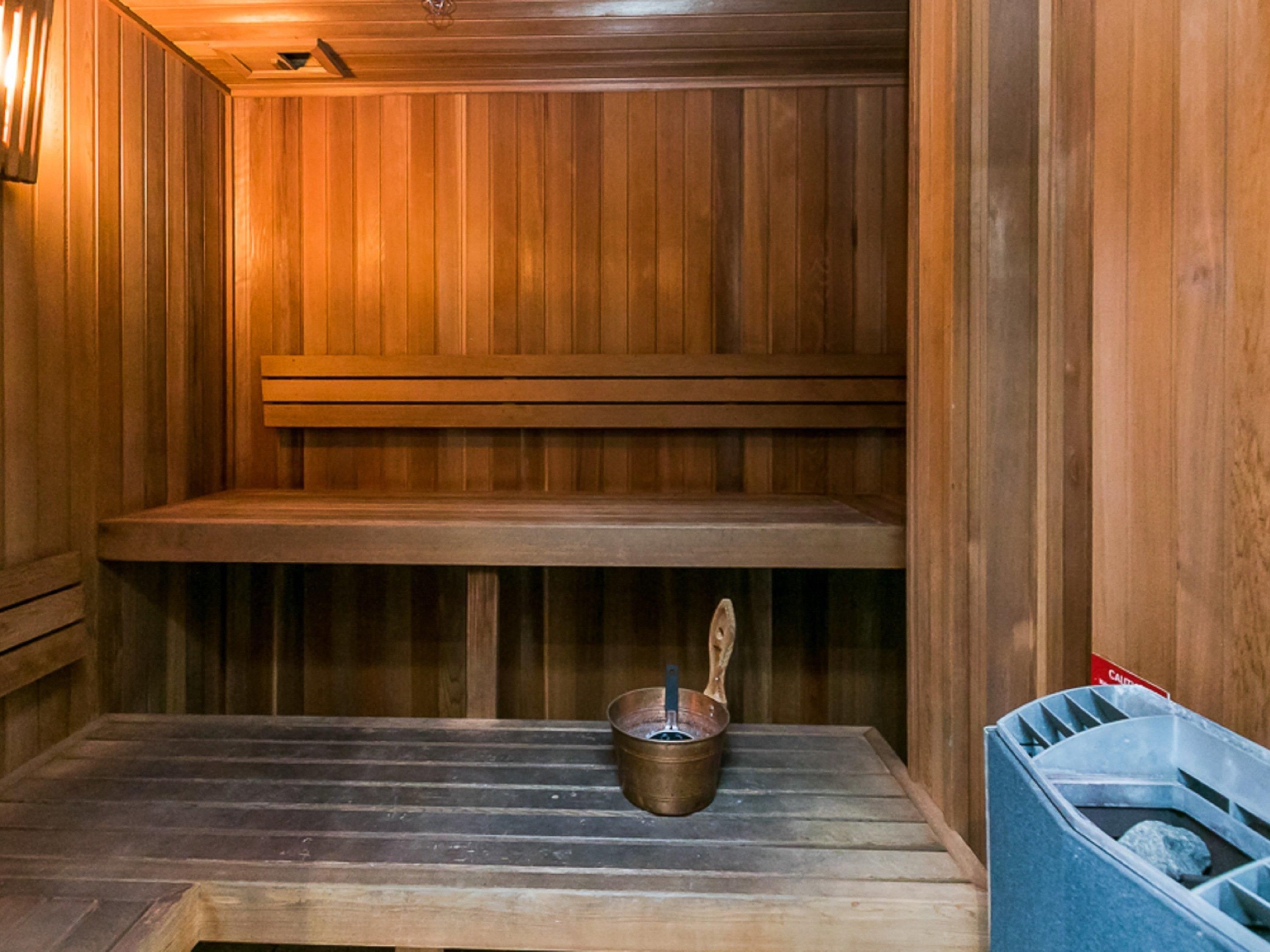 Uma sala de sauna com bancos de madeira, um balde de metal e uma lixeira.