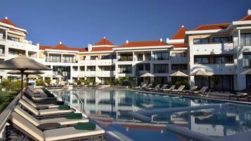 Área de piscina de hotel com espreguiçadeiras e guarda-sóis, rodeada por edifícios altos com varandas.