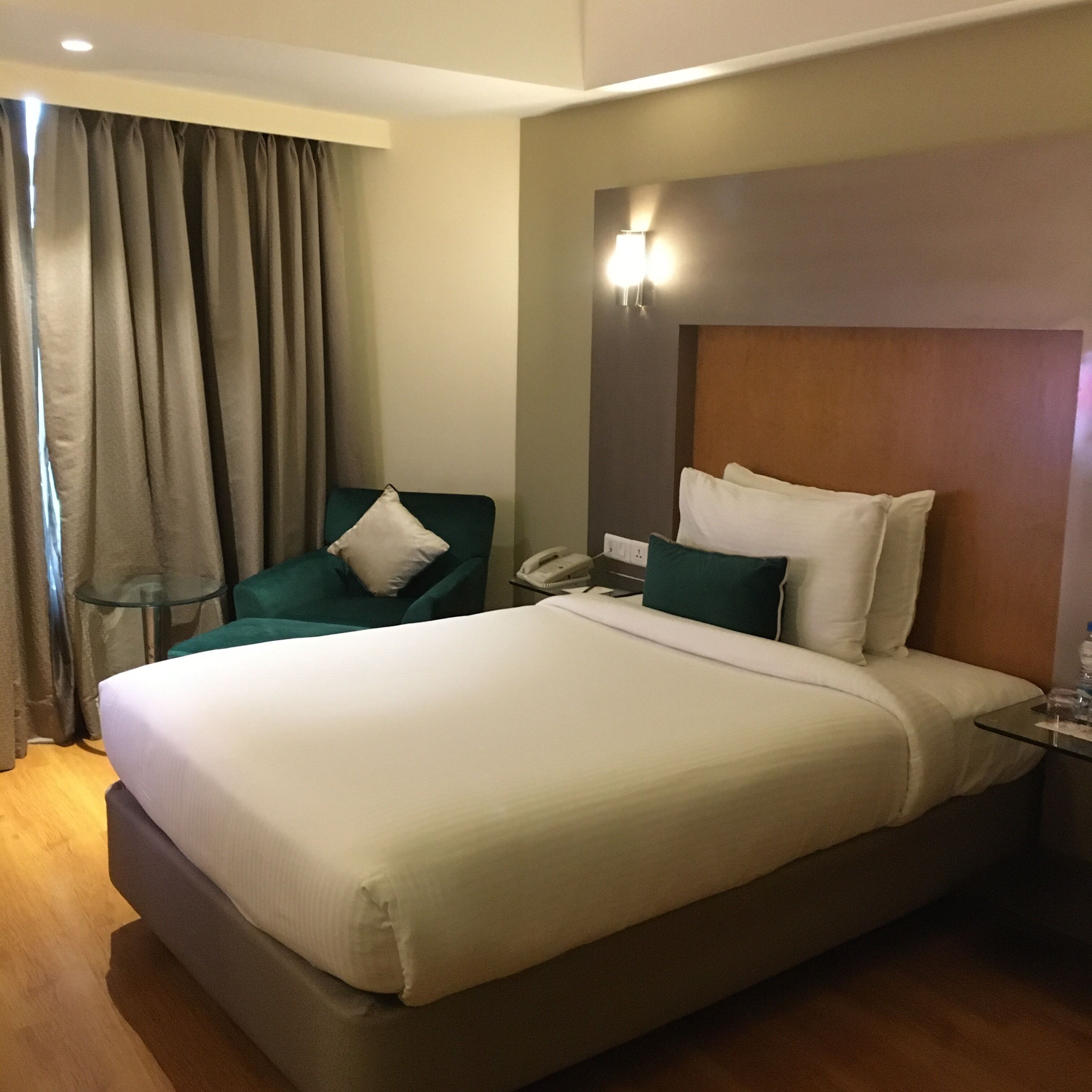 Quarto de hotel com uma cama grande, uma escrivaninha com telefone, uma cadeira e uma luminária.