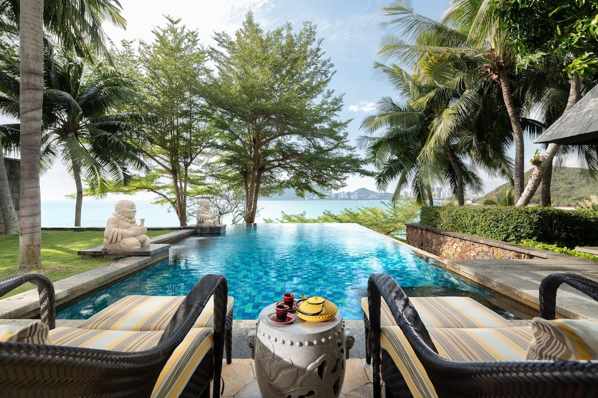 Área junto à piscina com cadeiras de vime, um vaso decorativo e vista para o mar.