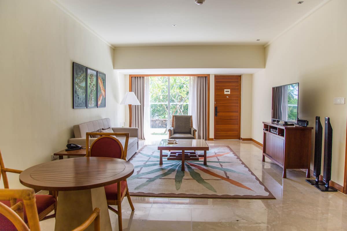 Quarto de hotel com área de refeições, sofá, televisão e uma janela grande.
