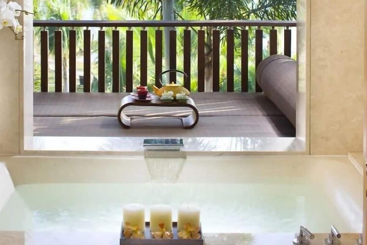 Uma banheira com vista para uma varanda, um vaso com flores e uma bandeja com chá e um bule.