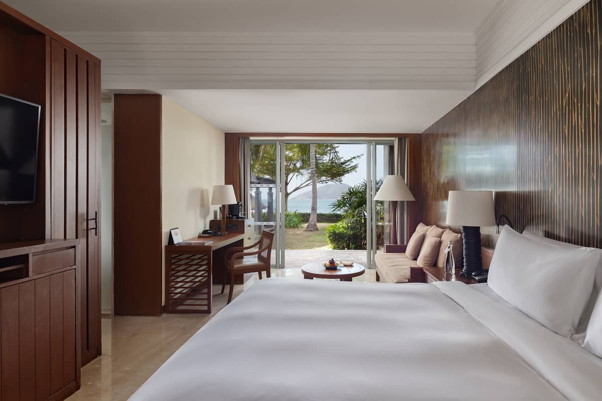 Quarto de hotel com uma cama grande, uma escrivaninha com cadeira, uma TV e vista para o exterior.