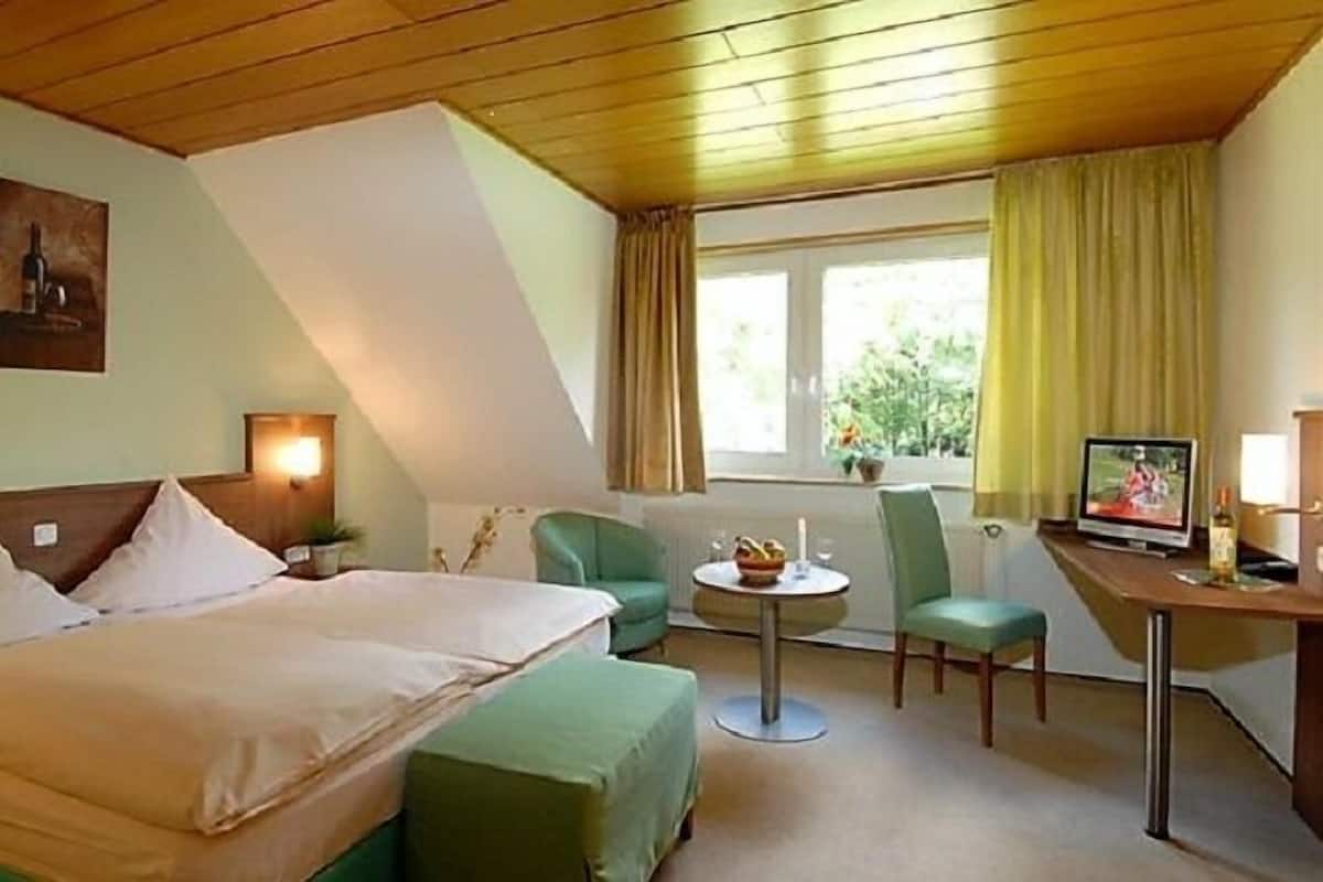 Quarto de hotel com cama, escrivaninha, cadeira e janela com cortinas.